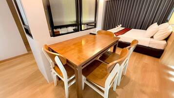 Quarto moderno com mesa de jantar de madeira e quatro cadeiras, um sofá e uma janela grande com persianas.