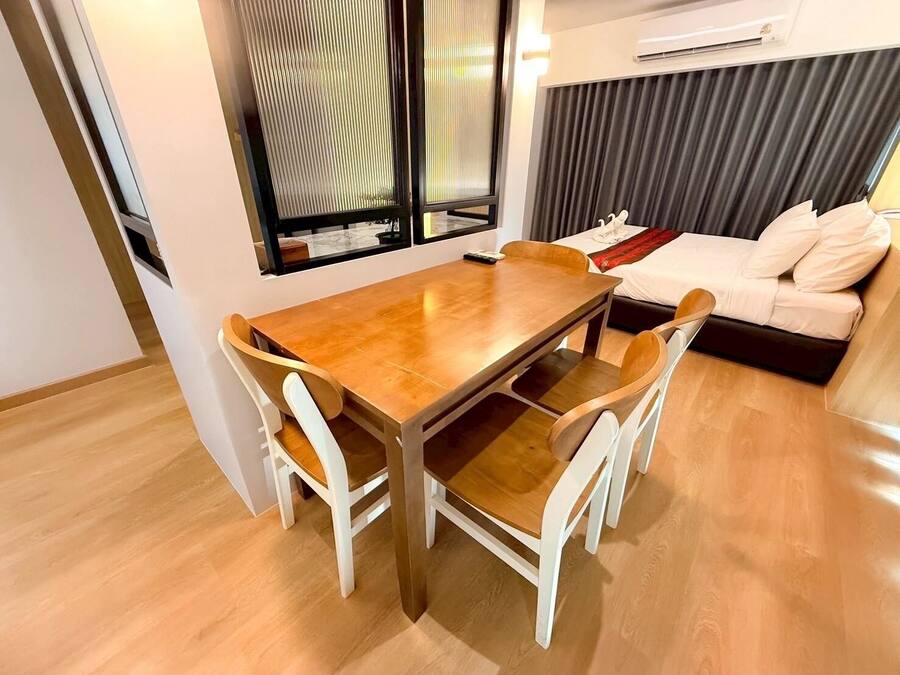 Quarto moderno com mesa de jantar de madeira e quatro cadeiras, um sofá e uma janela grande com persianas.