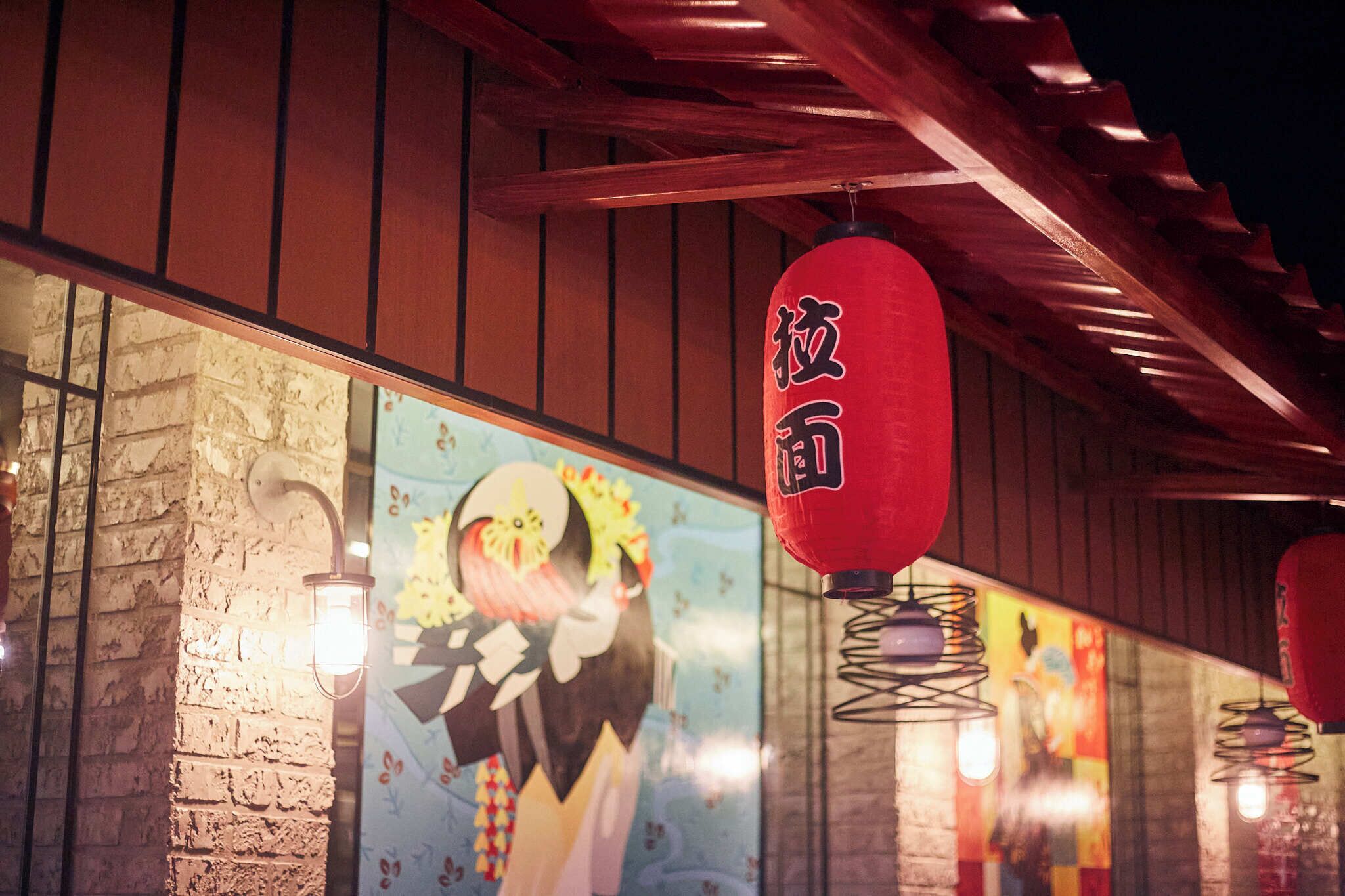 Interior de restaurante com paredes de tijolo aparente, lanternas vermelhas penduradas e um mural colorido na parede.