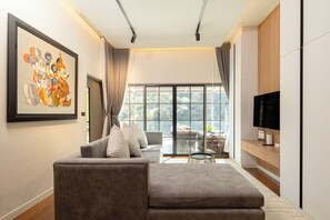 Uma sala de estar moderna com um sofá cinza, uma TV de tela plana e uma grande janela com cortinas.