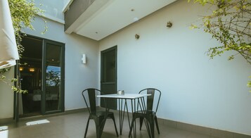 Um pátio externo com mesa e cadeiras, uma porta de correr de vidro e um pequeno acessório de iluminação fixado na parede.