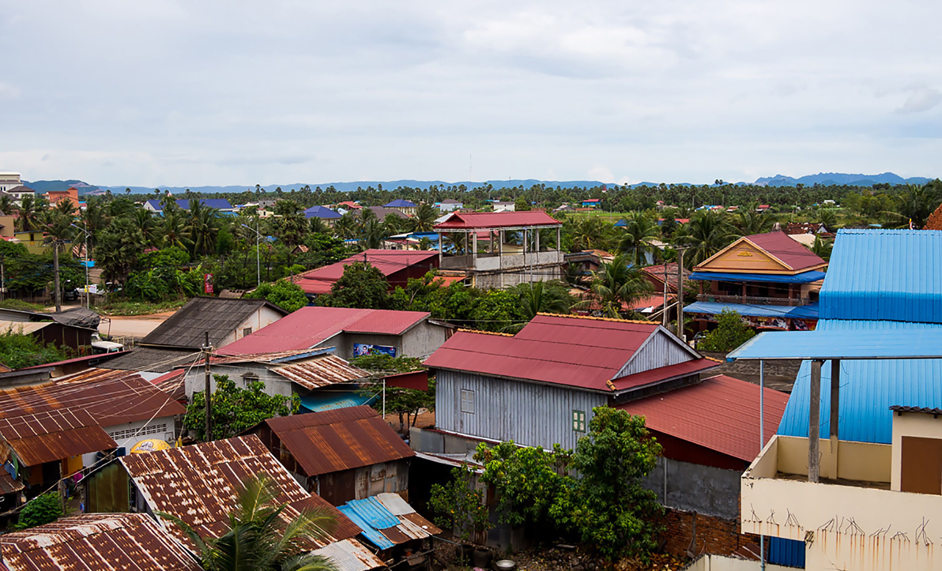 Uma área residencial densamente povoada com diversos edifícios, incluindo casas com telhados vermelhos e azuis, e uma construção notável com telhado vermelho e uma placa amarela.
