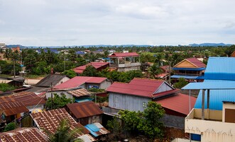 Uma área residencial densamente povoada com diversos edifícios, incluindo casas com telhados vermelhos e azuis, e uma construção notável com telhado vermelho e uma placa amarela.