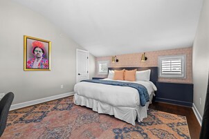 Quarto com cama, tapete estampado, luminária na parede e uma porta.