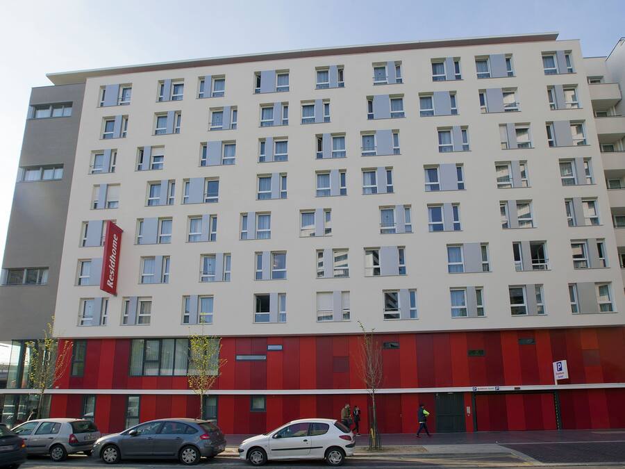 Um hotel de vários andares com fachada vermelha e branca, várias janelas e um sinal de estacionamento visível.