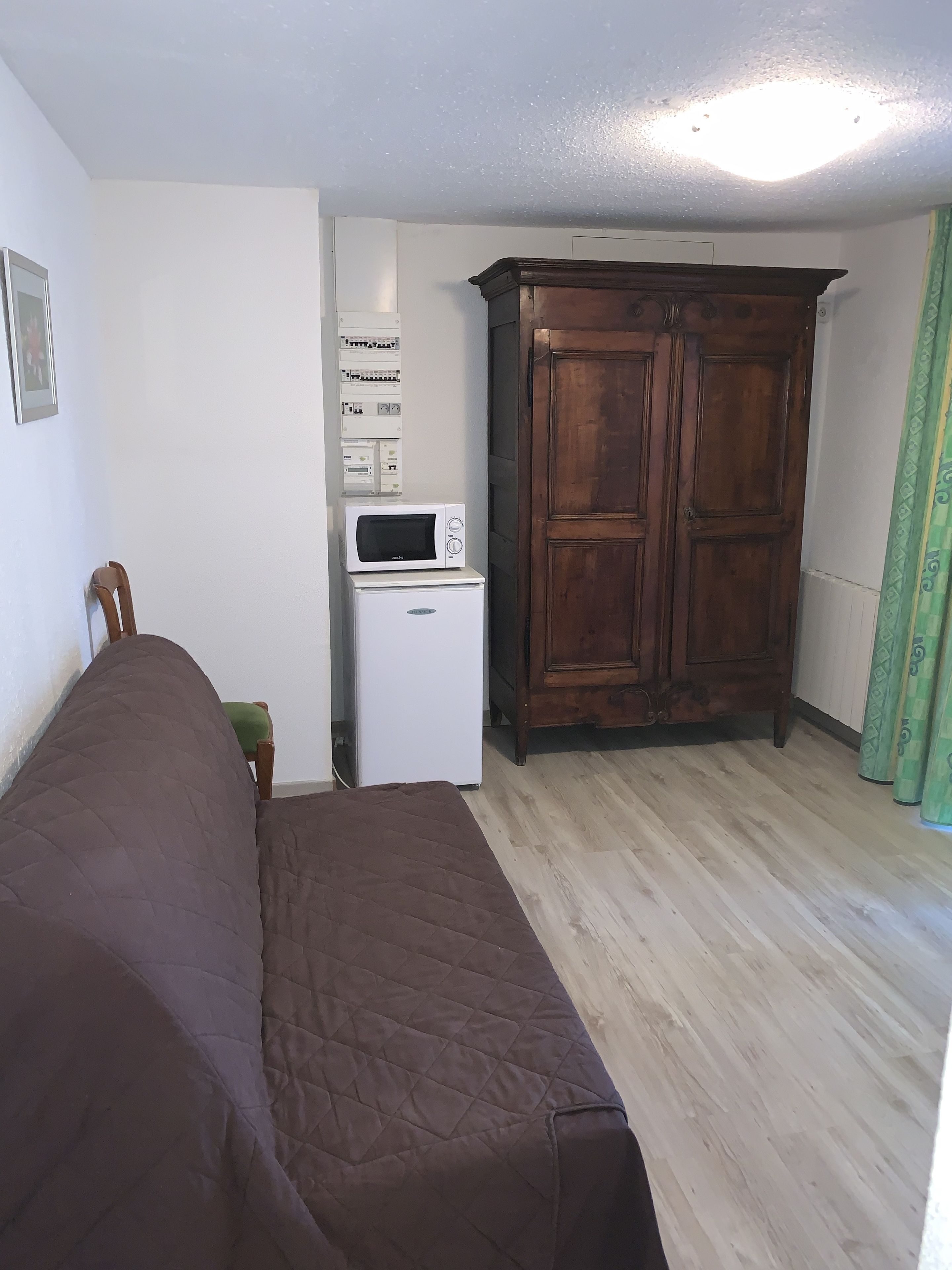 Quarto com uma cama, um frigorífico pequeno branco, micro-ondas e um guarda-roupa de madeira.