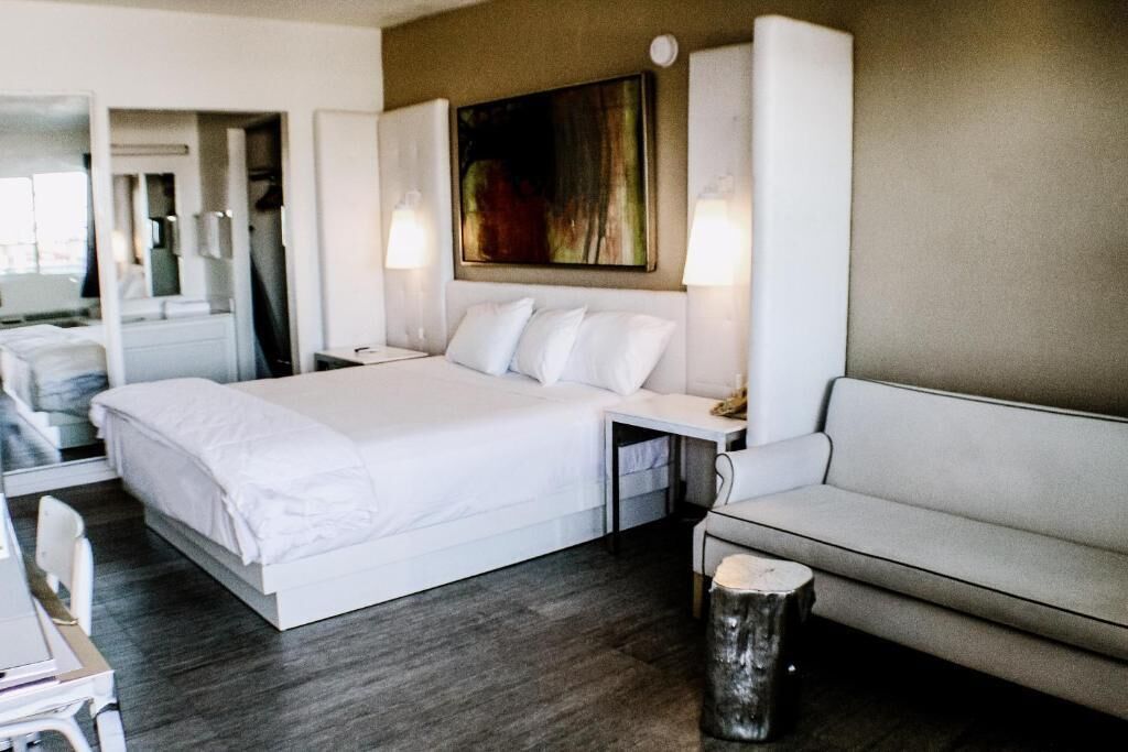 Quarto de hotel moderno com cama grande, sofá, escrivaninha e espelho.