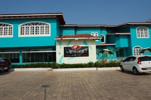 Um hotel com fachada turquesa, uma placa de identificação e área de entrada pavimentada.