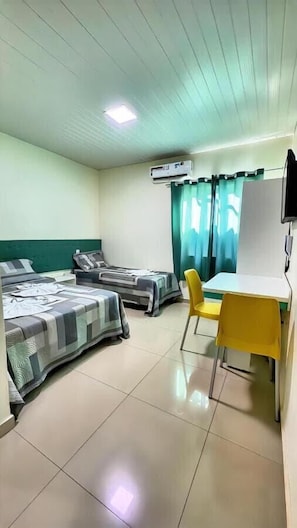 Quarto de hotel com duas camas, uma escrivaninha com cadeira, ar condicionado e televisão.