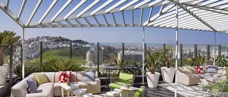 Terraço no telhado com pérgola branca, mobiliário de exterior e vista para a cidade.