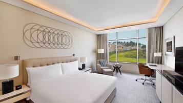 Quarto de hotel com uma cama grande, uma escrivaninha, uma cadeira, uma TV e vista para a cidade.
