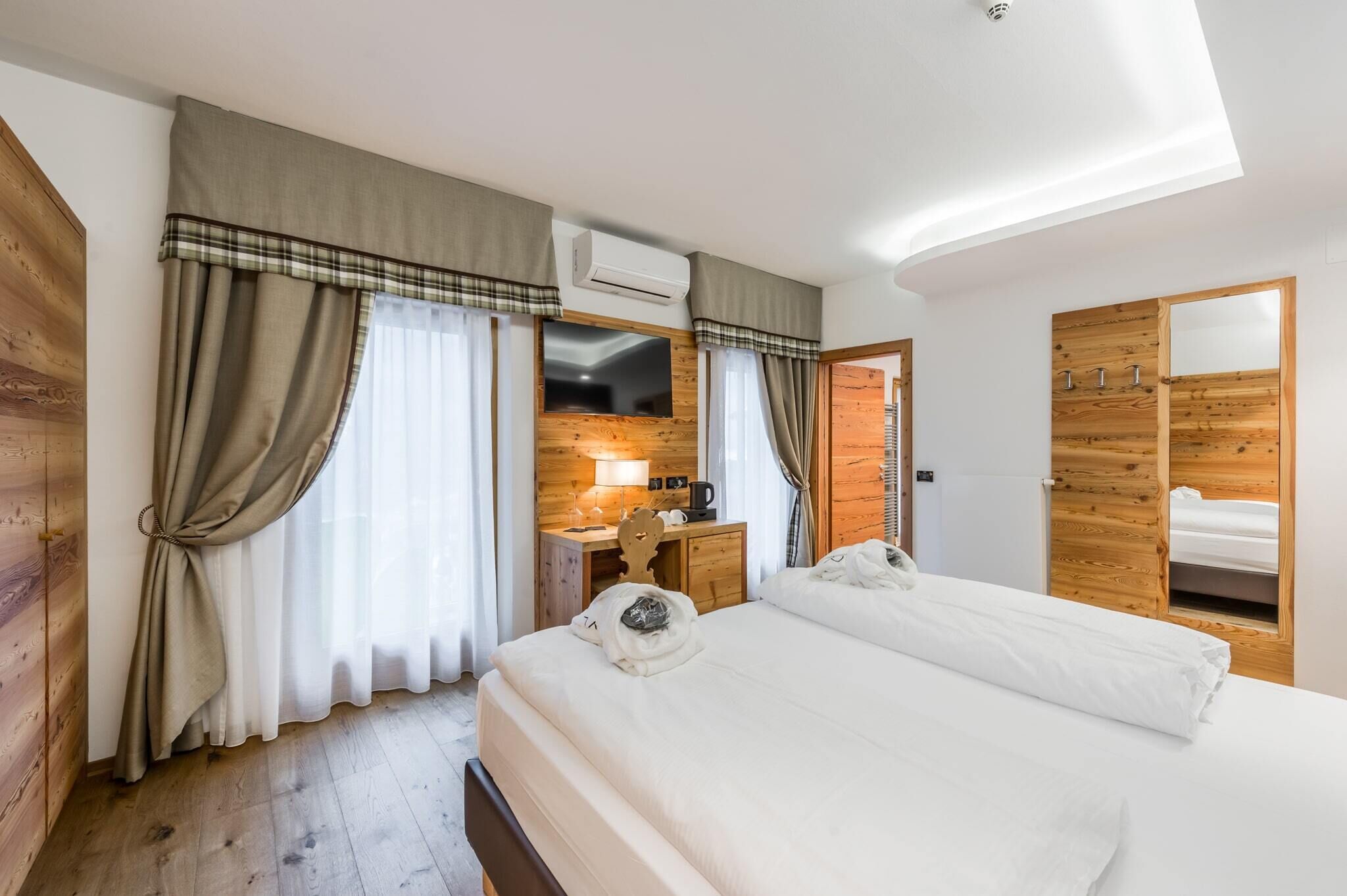 Quarto de hotel com cama, escrivaninha com luminária, espelho e guarda-roupa.