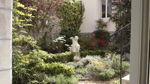 Estátua de pedra num jardim com um muro de pedra, diversas plantas e uma escadaria.