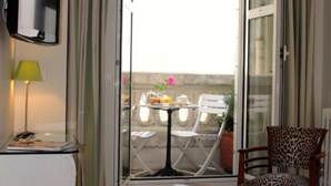 Quarto de hotel com cama, escrivaninha com luminária, televisão, poltrona e varanda com mesa e cadeiras.