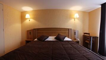 Quarto de hotel com uma cama grande, duas luminárias de cabeceira, um painel de madeira, mesa de cabeceira e uma cadeira.