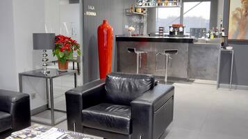 Uma área de bar moderna com um vaso vermelho, um sofá de couro preto e uma mesa de centro coberta de revistas.