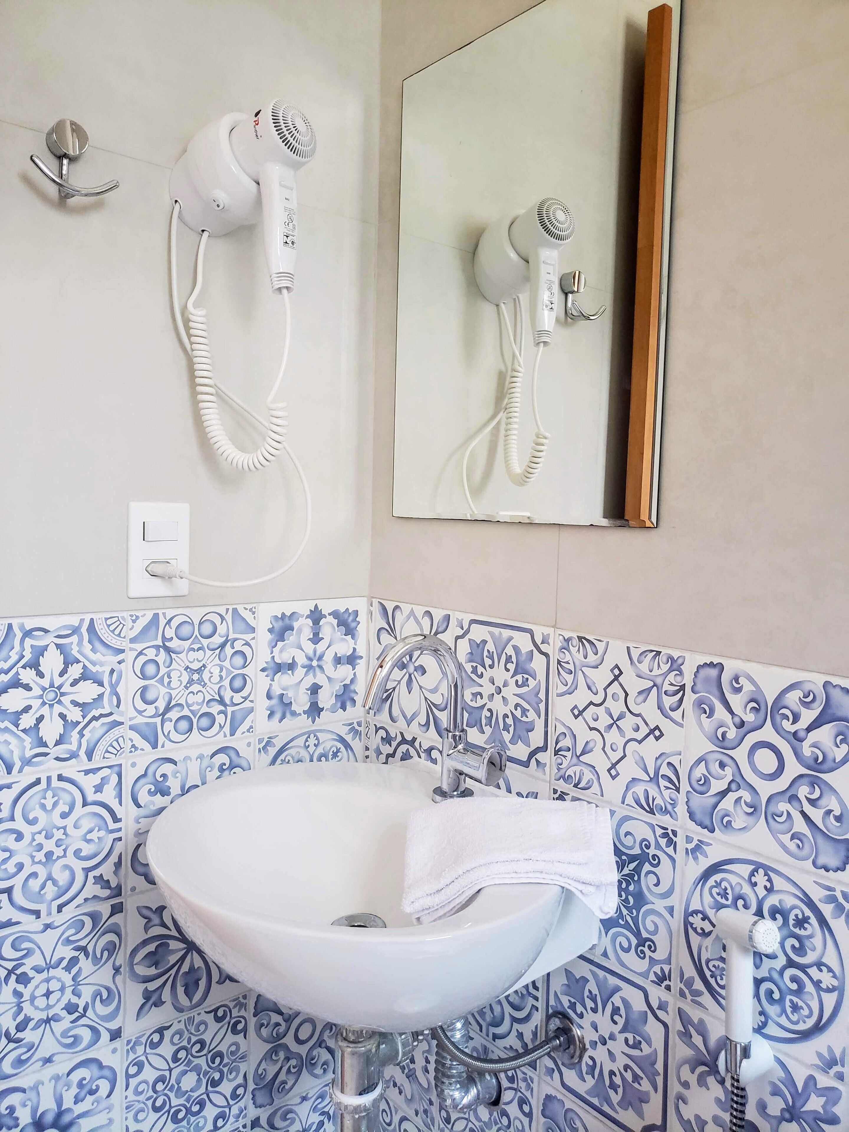 Casa de banho com lavatório branco, azulejos com padrão azul, secador de cabelo e espelho.