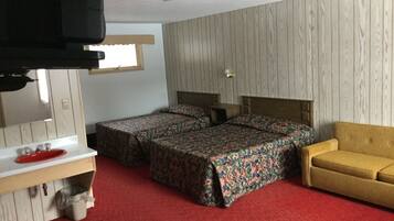 Quarto com duas camas, um tapete vermelho, cabeceira de madeira, sofá amarelo e pia branca.