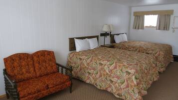Quarto de hotel com duas camas de solteiro, uma cadeira de madeira e mesa de cabeceira com abajur.