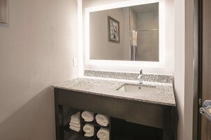 Casa de banho com lavatório de bancada em granito, espelho e porta-toalhas com toalhas dobradas.