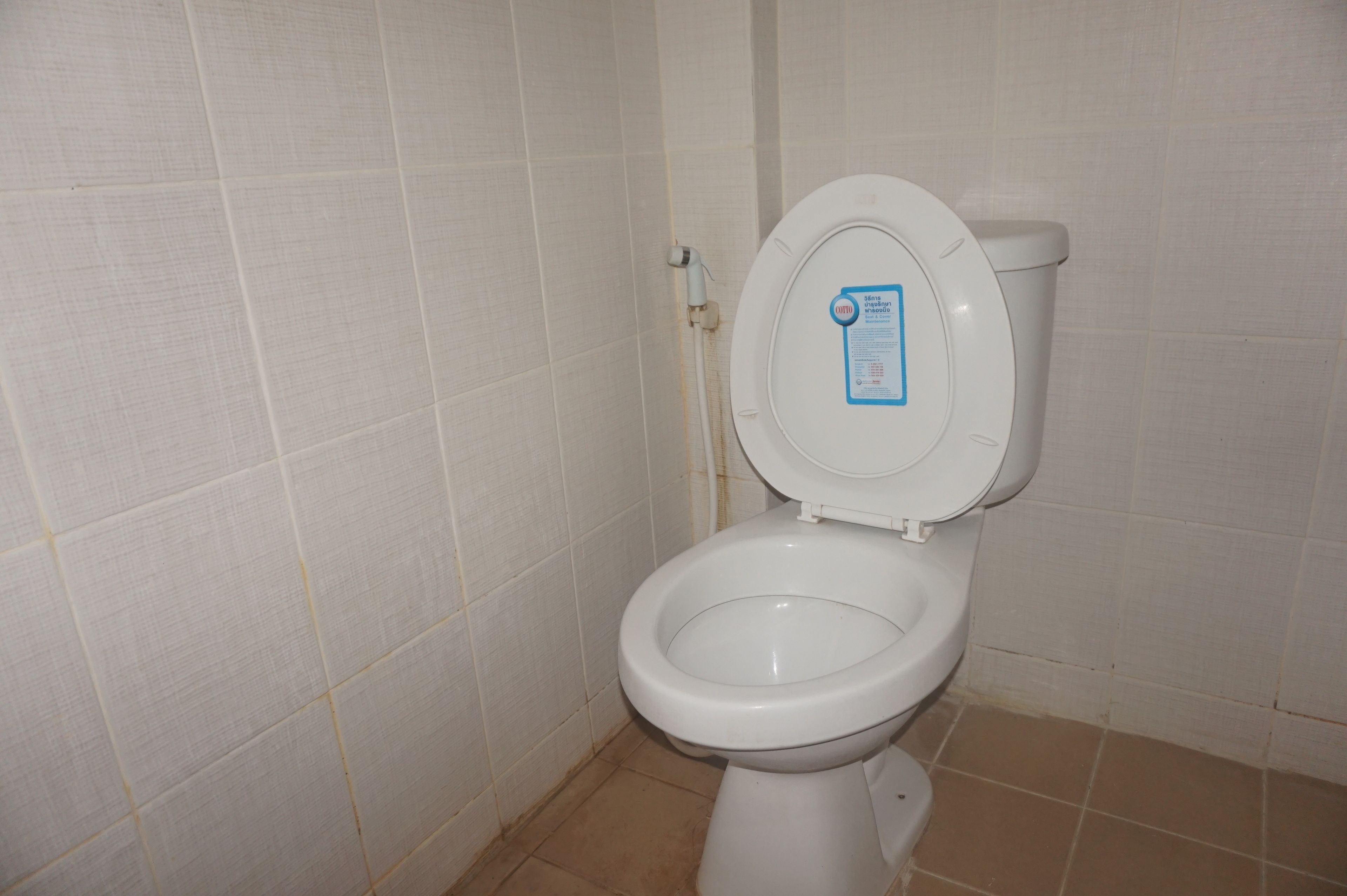 Sanitário branco com botão de descarga e etiqueta de manutenção.
