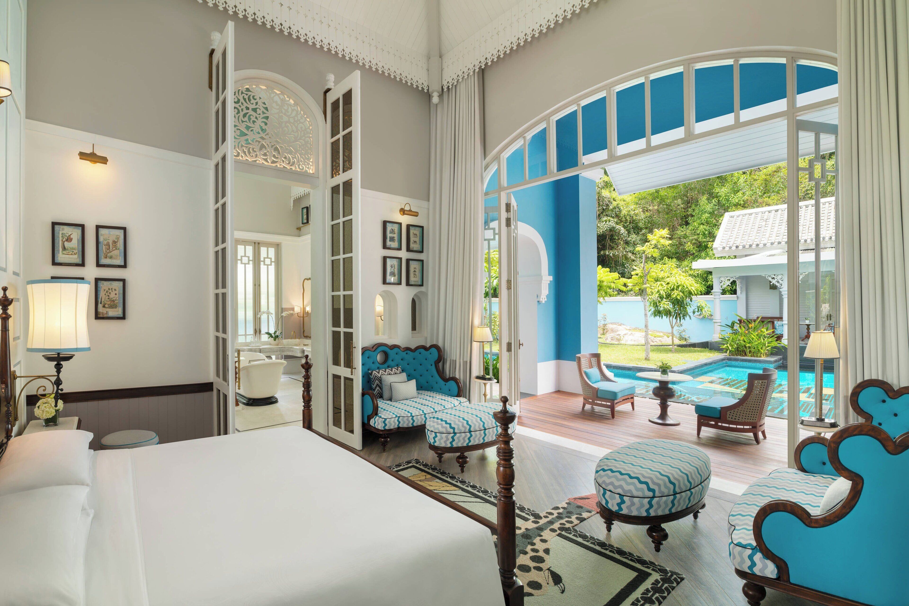 Um quarto espaçoso com uma cama grande, área de estar com cadeiras, vista para uma piscina e uma varanda.