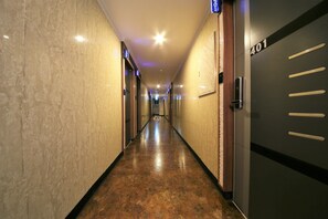 Corredor de hotel com piso de mármore, uma porta com a inscrição '401' e iluminação no teto.