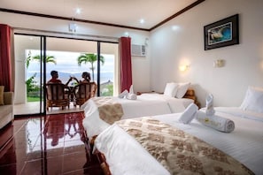 Quarto de hotel com duas camas, varanda com vista e área de refeições com duas pessoas.