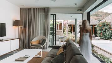 Quarto de hotel moderno com sofá, mesa de centro, TV e uma janela grande com vista para o exterior.