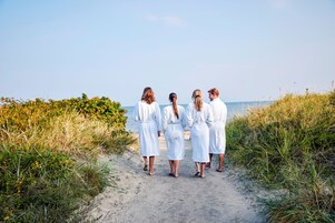 Uma trilha que leva à praia, com quatro pessoas vestindo túnicas brancas.