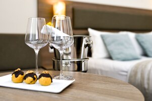 Uma mesa de jantar com duas taças de vinho, um prato branco com três doces, e uma chaleira de prata ao fundo.