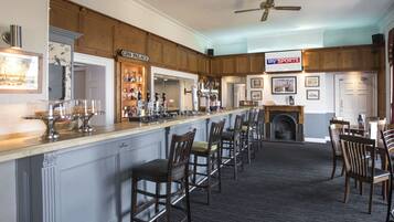 Uma área de bar com armários de madeira, um balcão com vitrines de vidro e uma placa com a inscrição 'Gin Palace'.