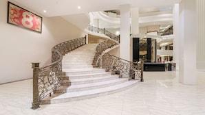 Uma escadaria imponente e curva, com grades de metal ricamente decoradas, que dá acesso a vários andares.