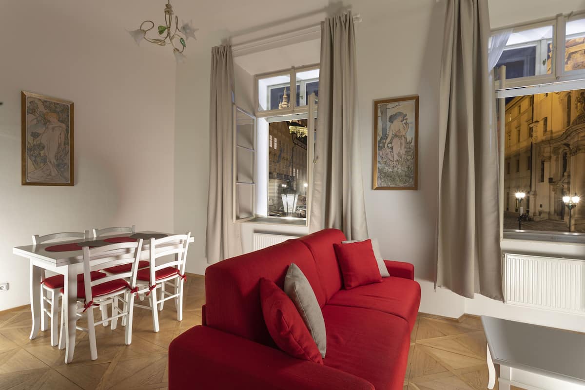 Quarto com sofá vermelho, mesa de jantar branca e cadeiras, além de uma janela com cortinas.