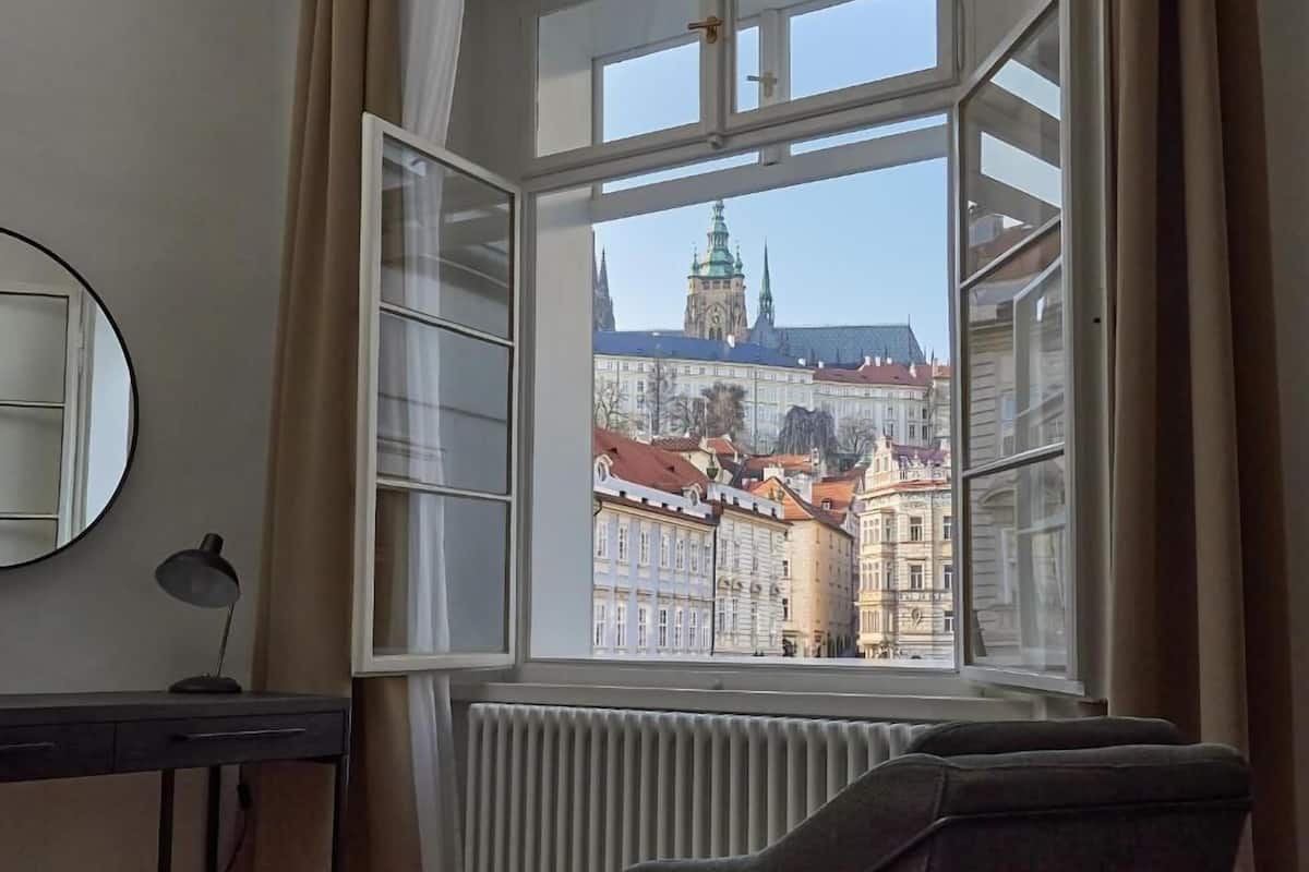 Quarto com uma janela ampla que oferece vista para edifícios históricos e uma torre imponente.