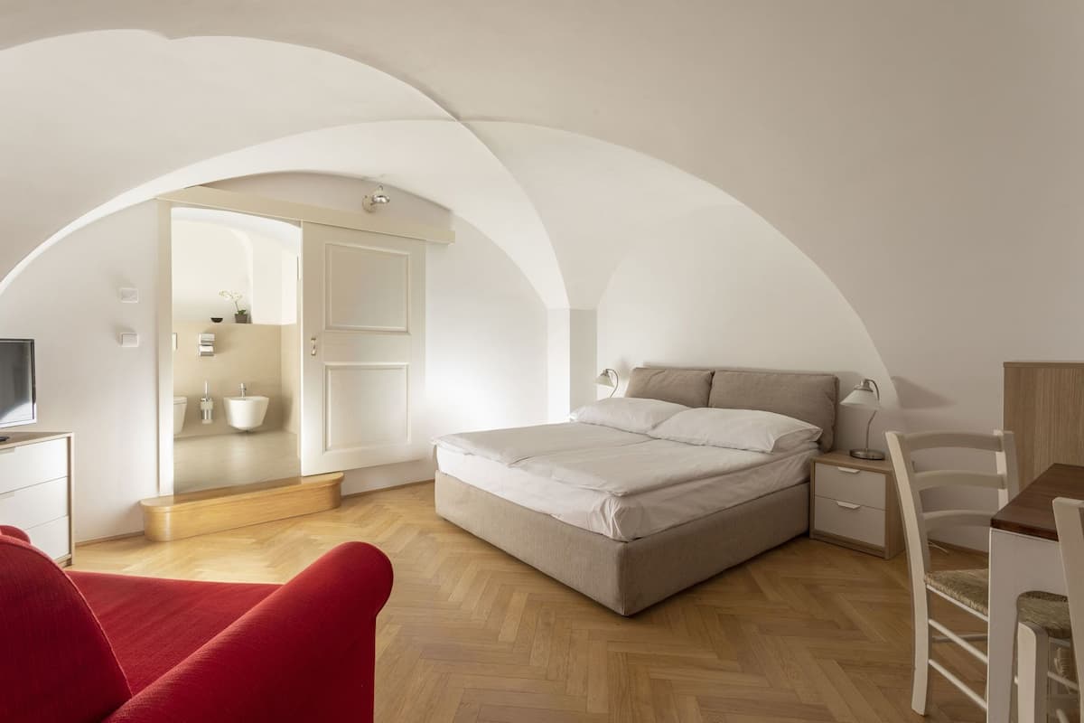 Quarto com cama, mesas de cabeceira, escrivaninha, cadeira e teto abobadado.