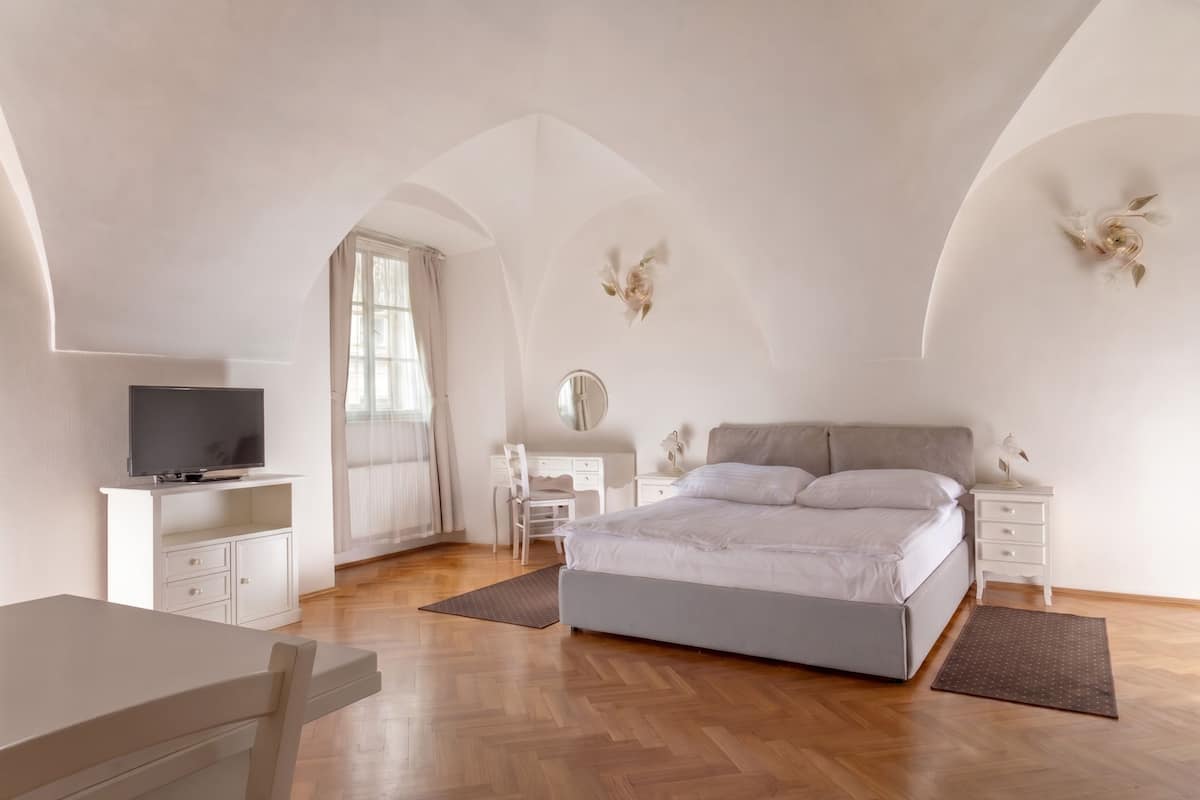 Quarto com cama, escrivaninha, cadeira, televisão e janela.