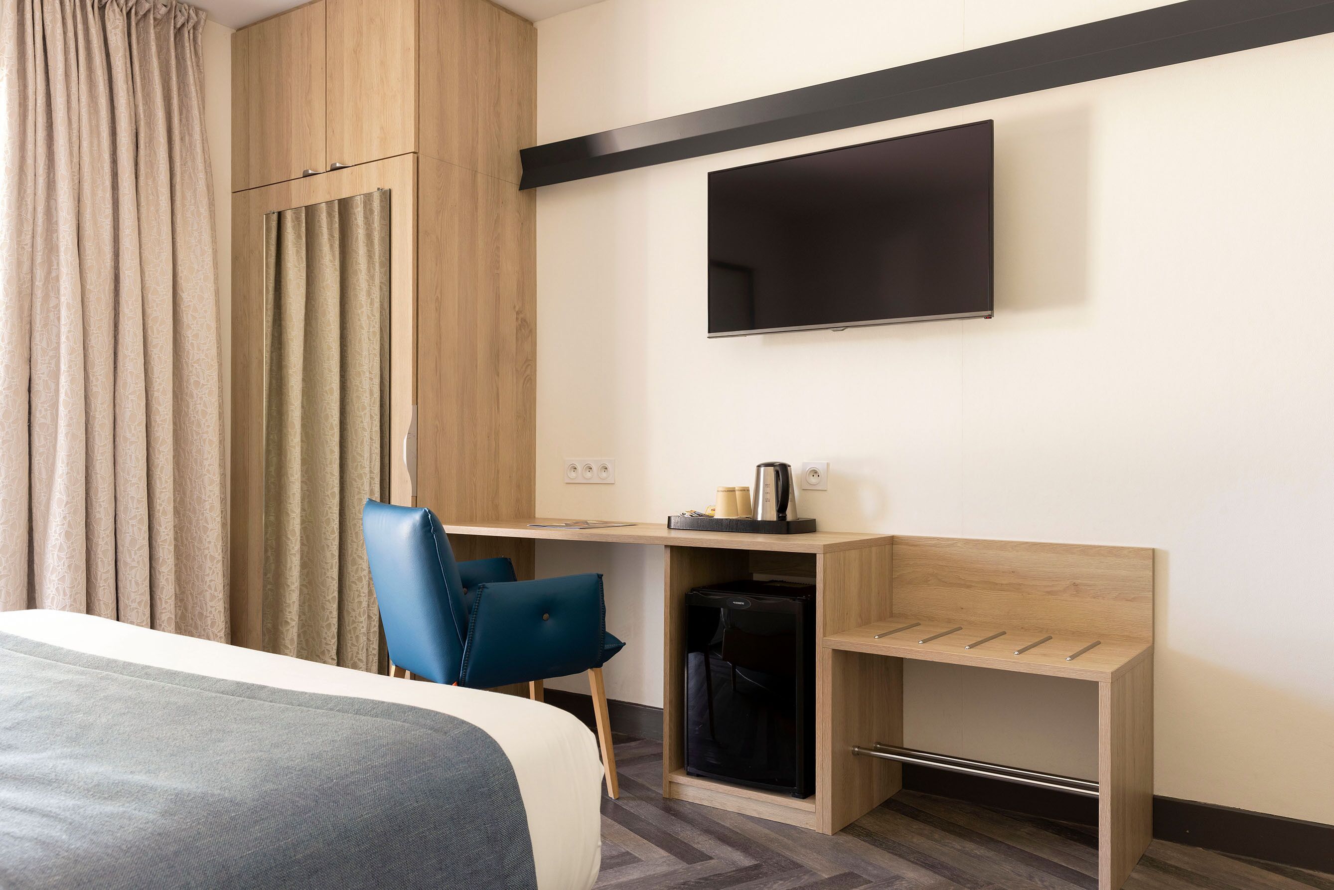 Quarto de hotel com cama, escrivaninha com computador, televisão e minibar.