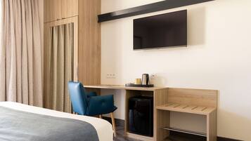 Quarto de hotel com cama, escrivaninha com computador, televisão e minibar.