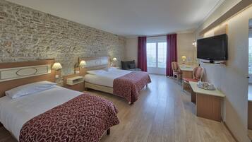 Quarto de hotel com duas camas, televisão, escrivaninha com cadeira e parede de pedra.