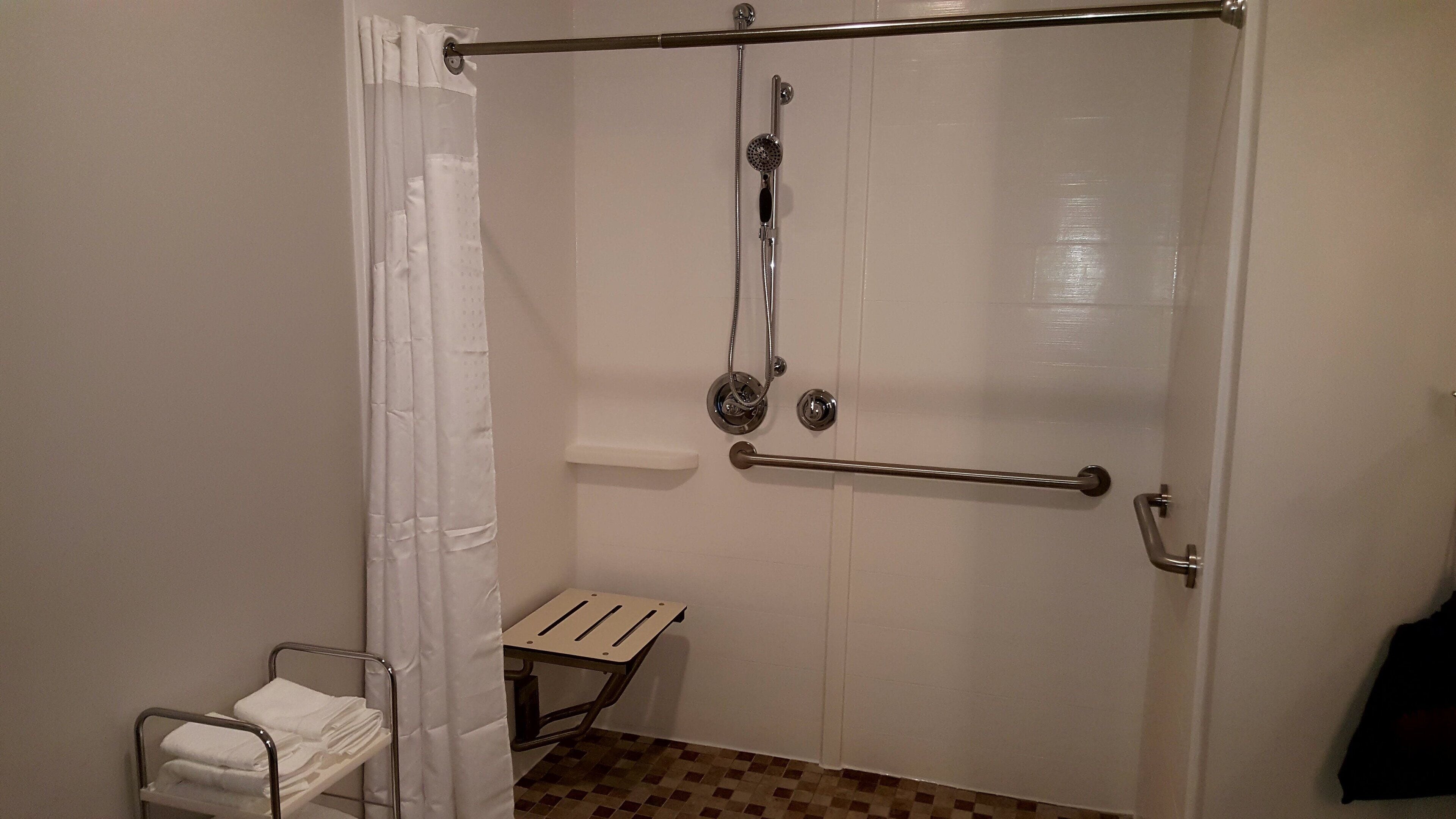 Área de duche com barra de apoio, um banco pequeno e suporte para toalhas.