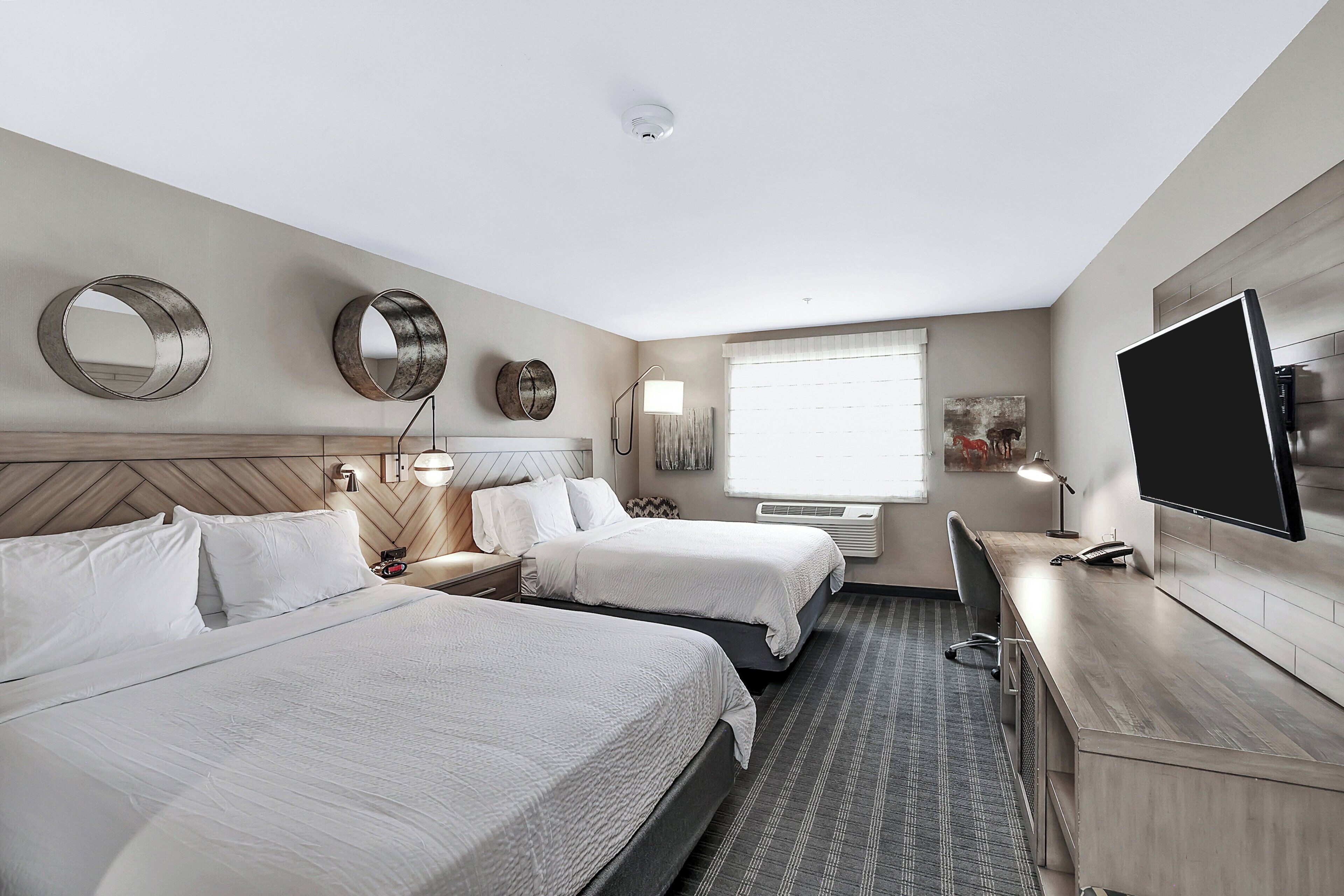 Quarto de hotel com duas camas, uma escrivaninha, televisão de tela plana e uma janela grande com persianas.