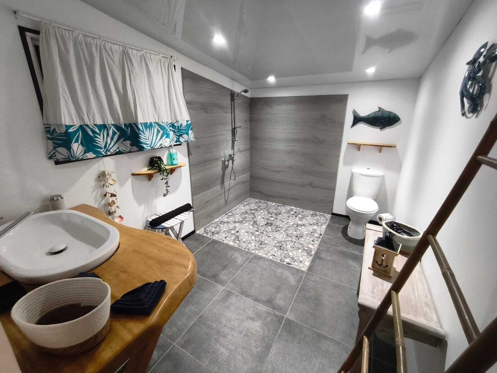 Uma casa de banho moderna com toucador de madeira, lavatório, chuveiro e sanita.