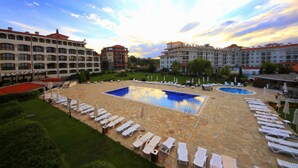 Um hotel com uma grande área de piscina, várias espreguiçadeiras e um pátio.