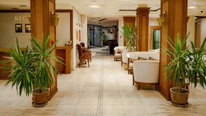Um hall de hotel com balcão de recepção, área de estar e plantas em vasos.