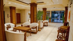 Um hall amplo com teto alto, grandes colunas de madeira e diversos assentos, incluindo sofás e cadeiras.