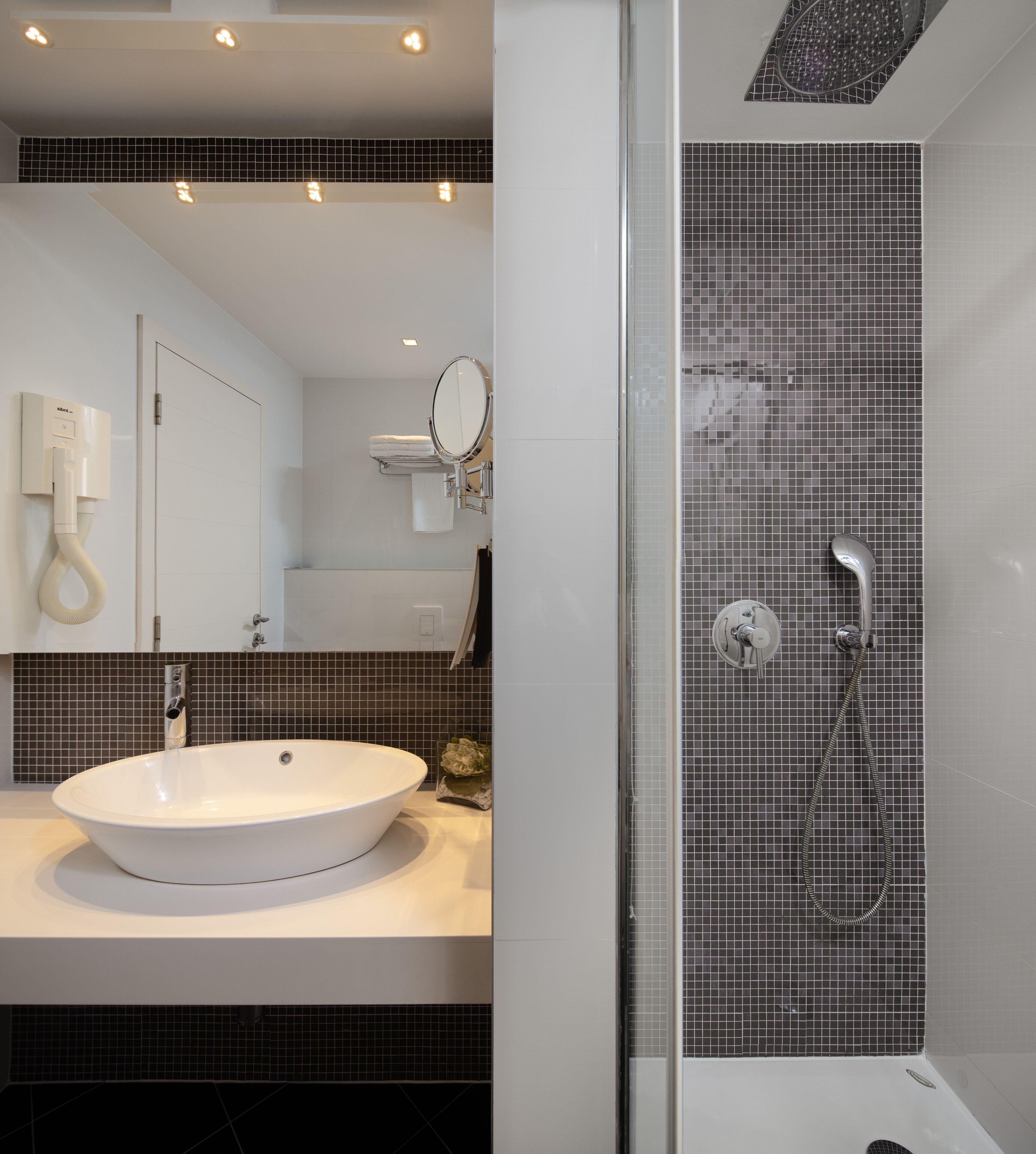 Um banheiro moderno com uma pia grande e branca, um chuveiro com proteção de vidro e um painel de azulejos.