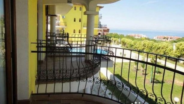 Uma varanda com guarda-corpo curvo, piscina e vista para um edifício e vegetação.