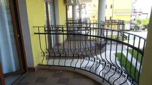 Guarda-corpo de metal curvo com chão de azulejos de pedra, levando a uma área externa coberta com uma parede amarela e vista para uma rua residencial.
