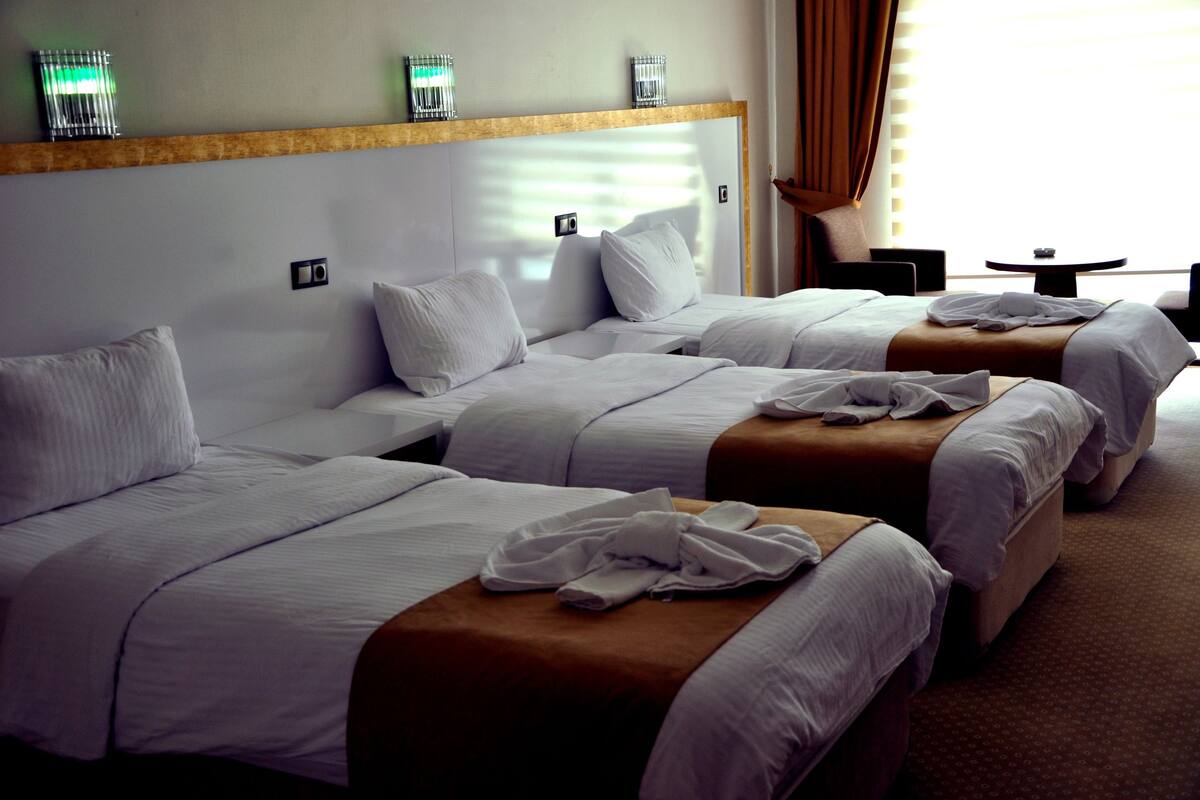 Quarto de hotel com duas camas, uma mesinha e uma janela com cortinas.